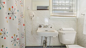 Casa de banho com lavatório branco, sanita e secador de cabelo na parede.