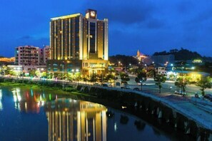 Um hotel alto com vários andares, um reflexo na água e uma ponte em primeiro plano.