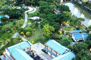 Um parque com caminhos, um lago e edifícios com telhados azuis.