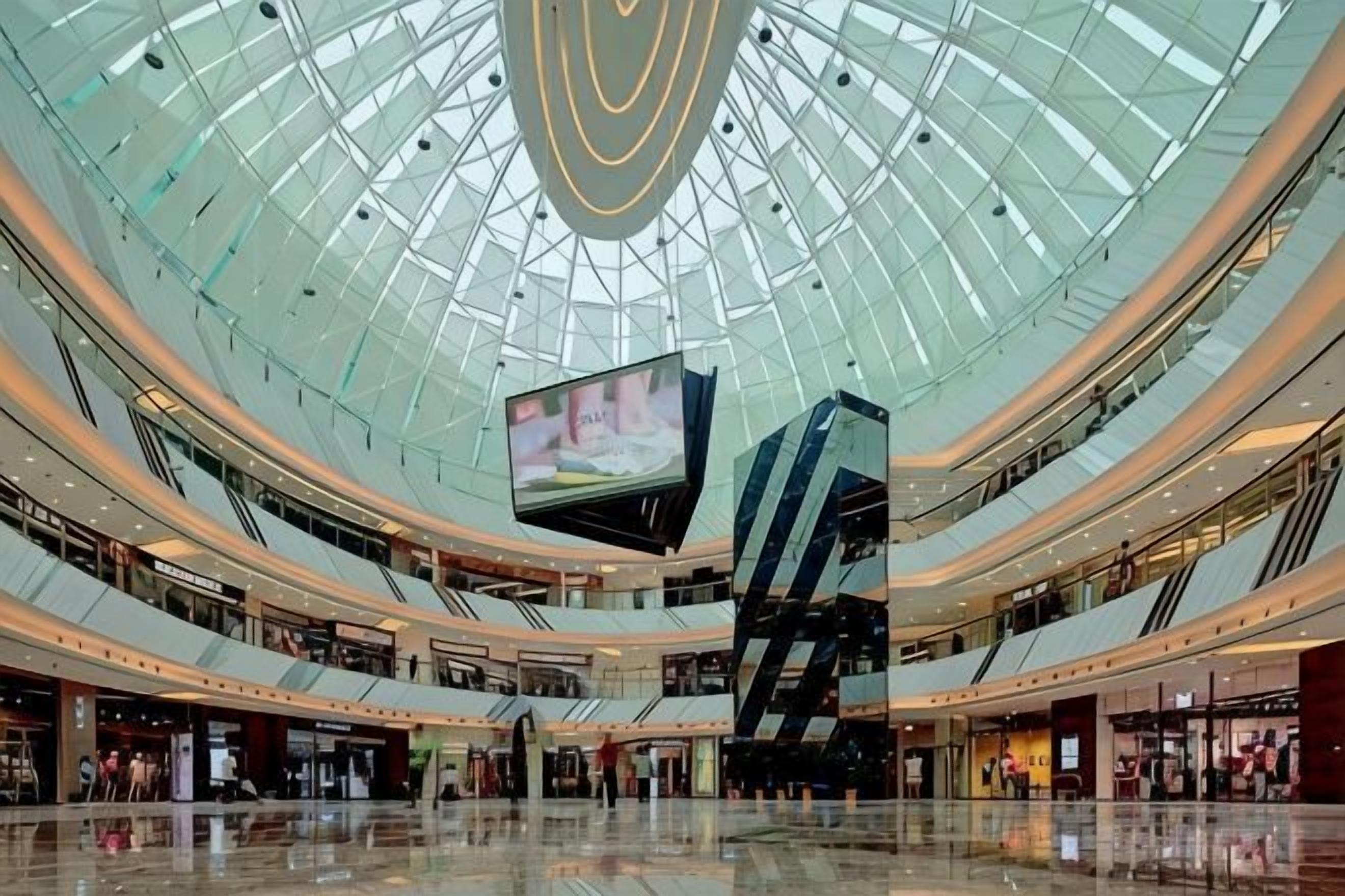 Um grande shopping com vários andares, um átrio central, escadas rolantes e um painel digital enorme.