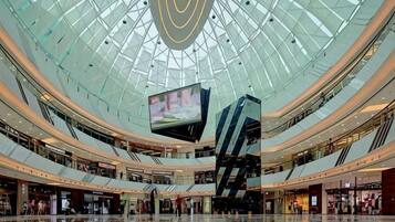 Um grande shopping com vários andares, um átrio central, escadas rolantes e um painel digital enorme.
