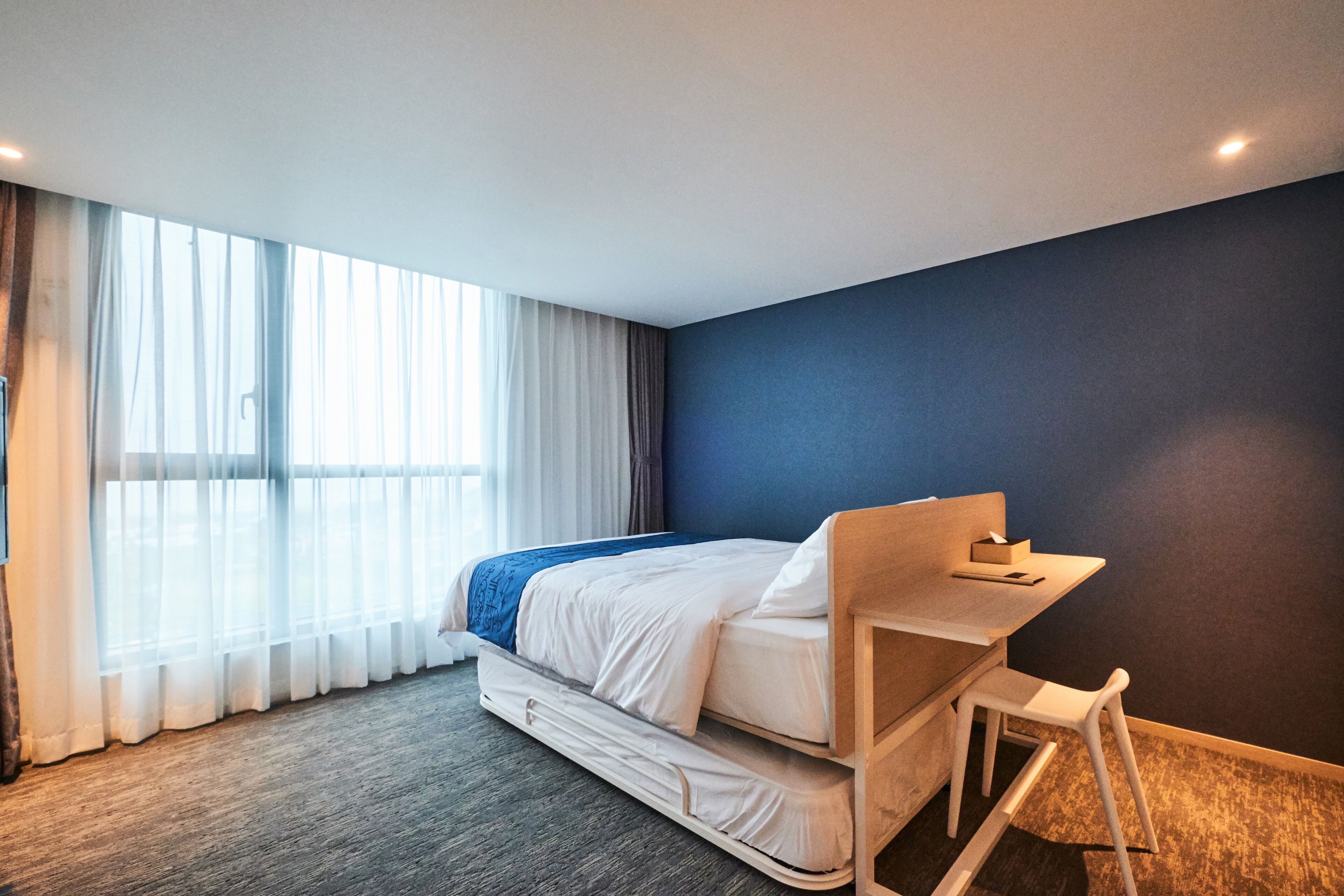 Quarto de hotel moderno com uma cama, uma escrivaninha e uma cadeira.
