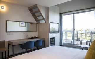 Quarto de hotel moderno com uma cama grande, uma escrivaninha com duas cadeiras, uma televisão de tela plana, uma janela ampla com varanda e uma escada.