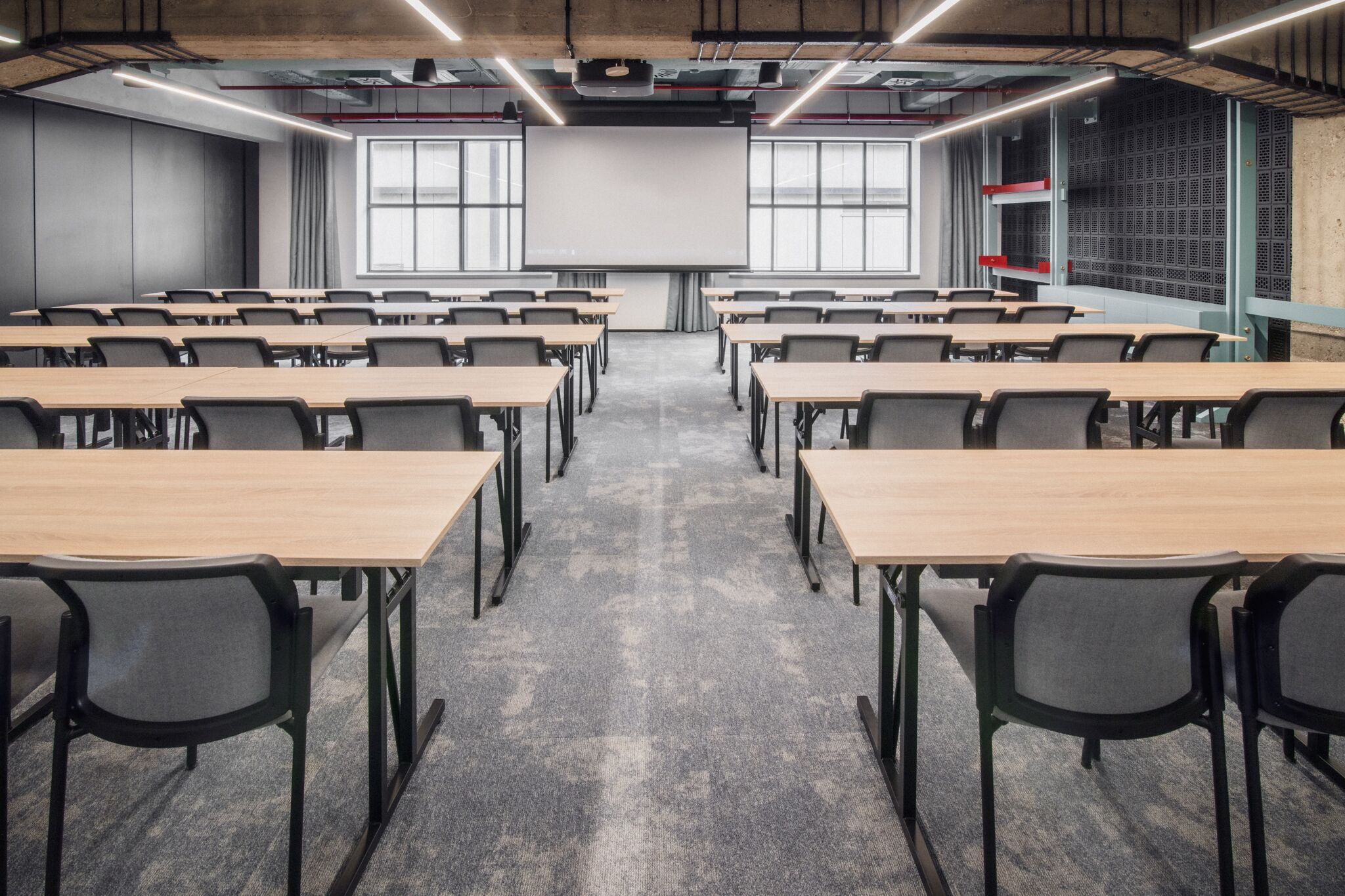 Sala de conferências com várias mesas e cadeiras, amplas janelas e tela de projeção.