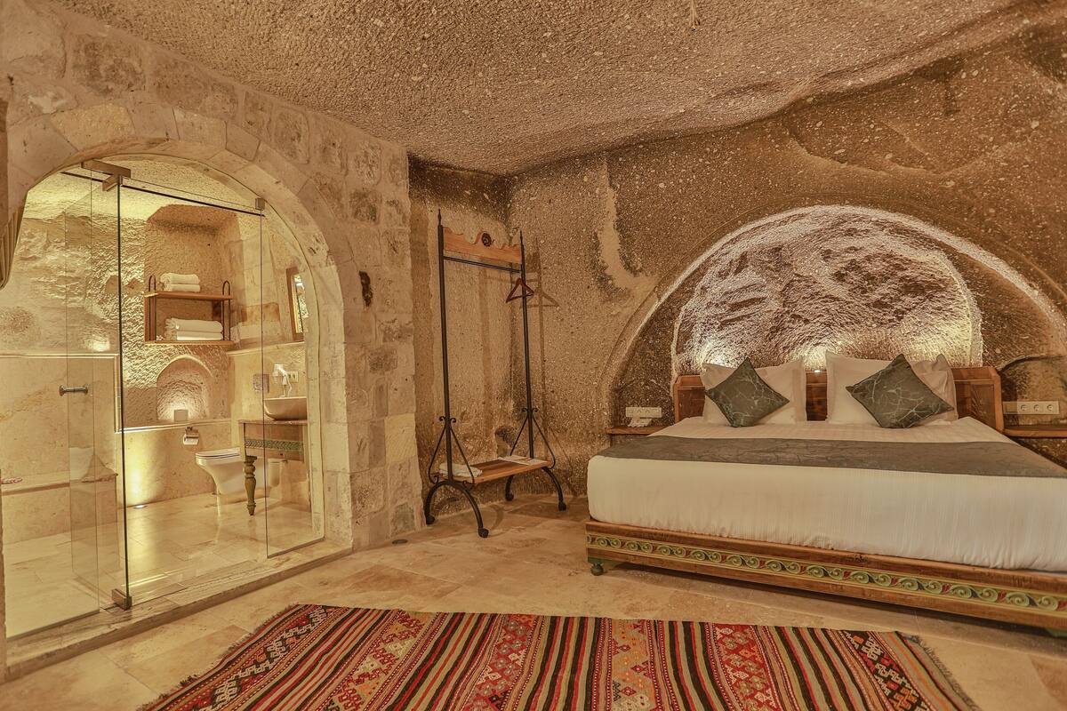 Quarto com uma cama grande, banheiro envidraçado e parede de pedra.