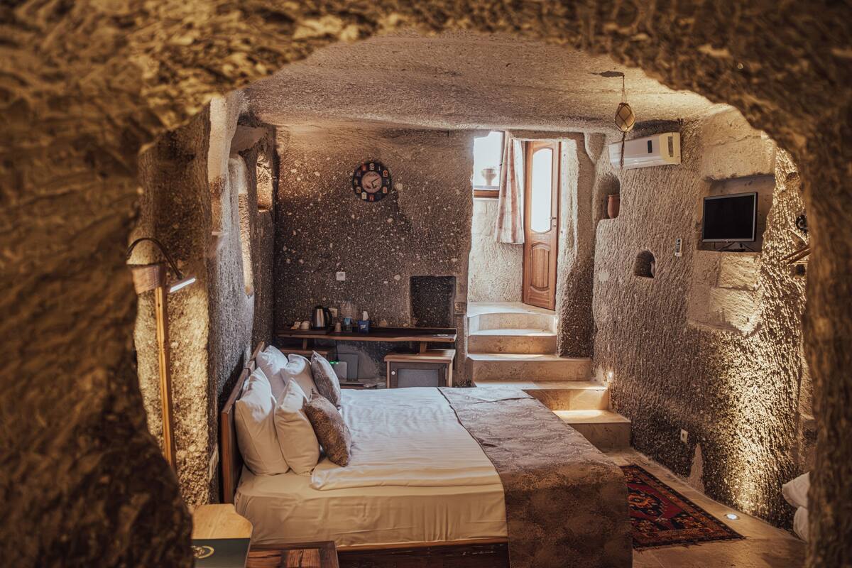 Um quarto acolhedor e rústico com uma cama, uma escrivaninha pequena, uma televisão e um relógio na parede.
