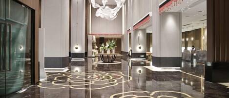 Um hall de hotel moderno com piso de mármore polido, uma área de estar central e um grande lustre.
