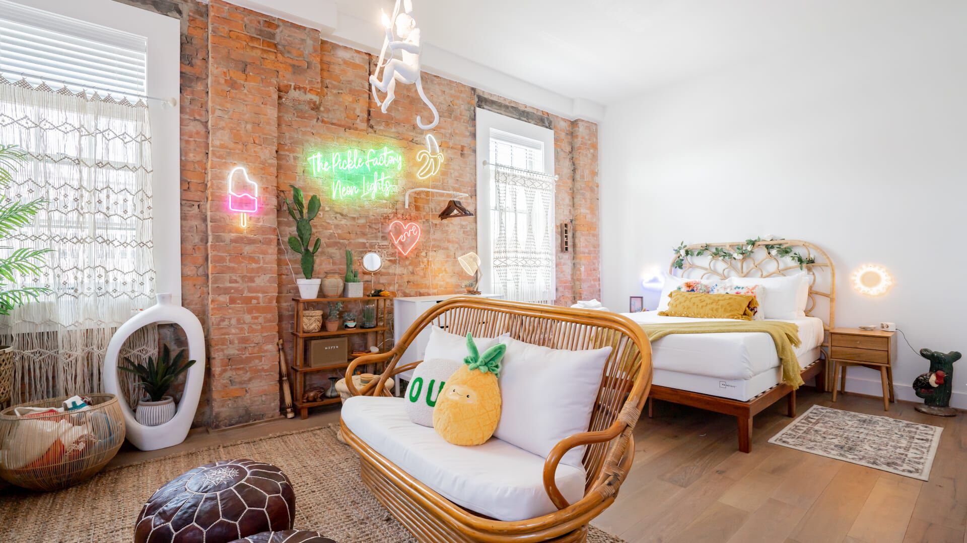 Um quarto aconchegante com parede de tijolos, duas camas, uma cadeira de vime e um letreiro neon.