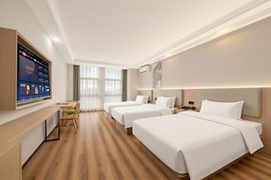 Quarto de hotel com três camas, uma escrivaninha e uma televisão.