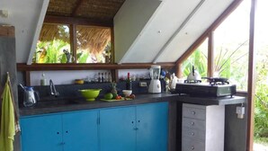 Cozinha com armários azuis, bancada preta e janela com vista para o verde.