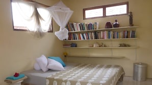 Um quarto com cama, mesa de cabeceira, estante de livros e janela com cortinas.