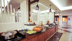 Disposição de buffet com diversos alimentos e bebidas, um balcão de madeira e luminárias pendentes.