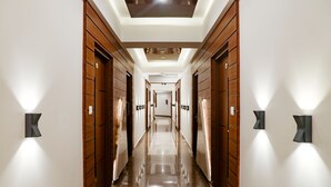 Um corredor longo e bem iluminado, com portas de madeira e luminárias fixadas na parede.