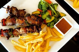 Um prato com espetos de carne grelhada, batatas fritas e uma porção de legumes variados acompanhada de molho.