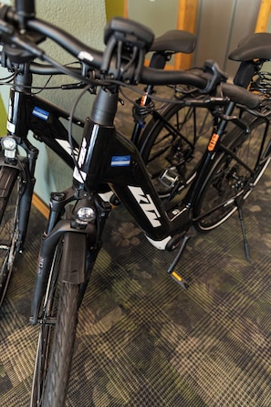 Close-up de uma bicicleta com estrutura preta e marca branca, posicionada em ambiente interno com piso de carpete estampado.