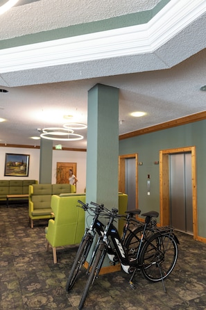 Um hall com assentos verdes, um elevador e bicicletas.