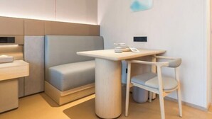 Quarto moderno e minimalista com um sofá de cor clara, uma mesinha com uma cadeira e um candeeiro fixado na parede.