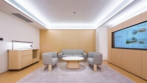 Sala de conferências moderna com mesa redonda, quatro cadeiras cinzentas, uma tela grande e painéis de madeira.