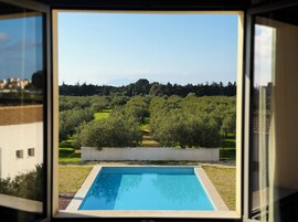Piscina com vista para oliveiras e uma paisagem distante.