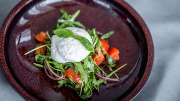 Um prato de cerâmica escura com uma salada de folhas verdes, tomates e um pouco de molho branco.
