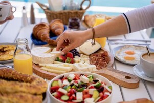 Uma mesa de café da manhã com diversos queijos, frutas, croissants e uma saladeira.