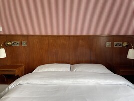 Quarto de hotel com cabeceira de madeira, duas mesas de cabeceira com abajures e cama com roupa de cama branca.