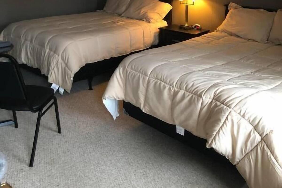 Quarto de hotel com duas camas de solteiro, uma escrivaninha, uma cadeira e um abajur.