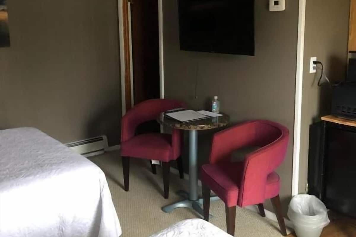 Quarto de hotel com duas camas, televisão, uma pequena mesa com cadeiras e um cesto de lixo.