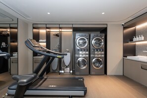 Quarto de hotel moderno com esteira, máquina de lavar e banheiro bem organizado.