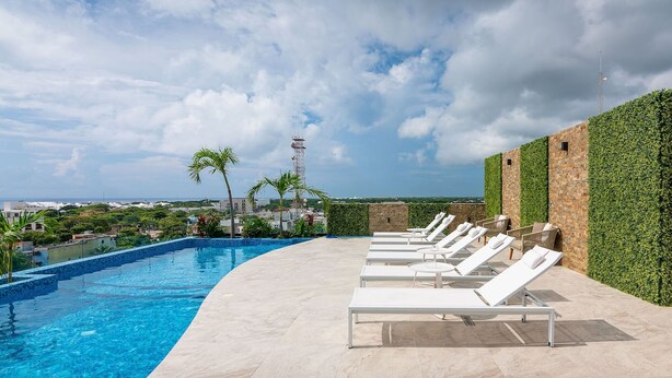 Piscina com espreguiçadeiras, vista da cidade e parede verde.