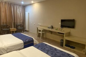Quarto de hotel com duas camas, uma escrivaninha, uma cadeira, uma televisão e um sapateiro.