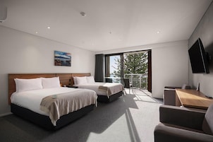 Quarto de hotel com duas camas, uma mesa de escritório, uma cadeira, televisão e varanda com vista para árvores.