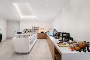 Interior moderno de café com balcão longo, máquinas de café e diversos itens de comida expostos.