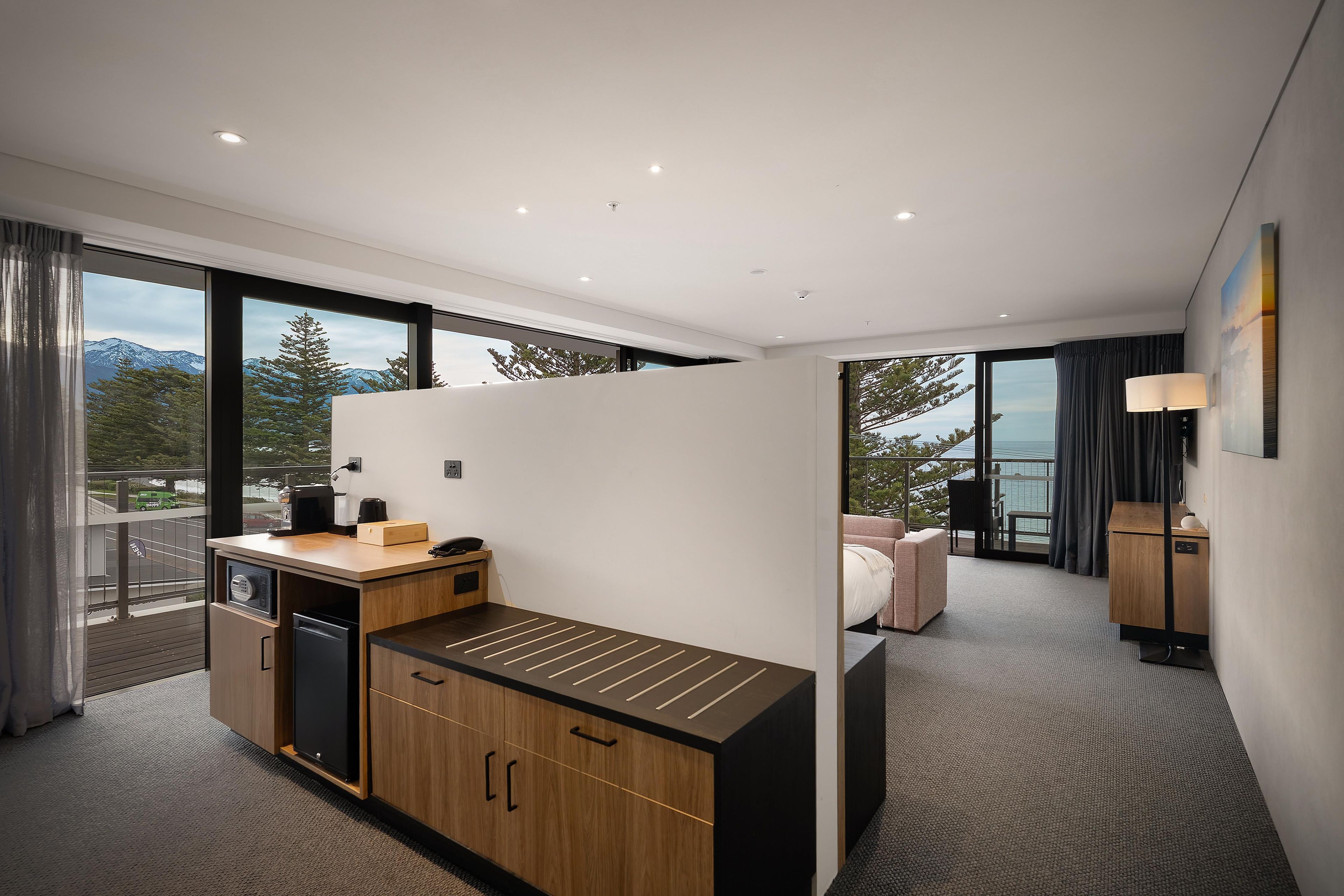 Quarto de hotel moderno com cozinha compacta, varanda com vista para montanhas e área de estar com vista para o mar.