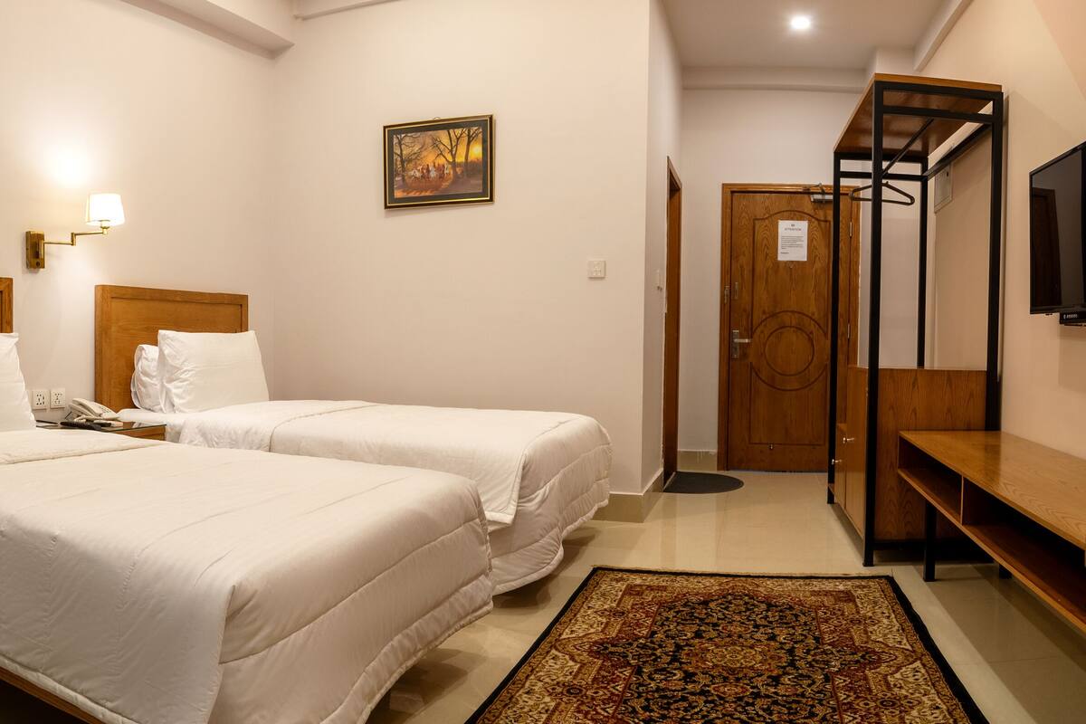 Quarto de hotel com duas camas, uma mesa de jantar com frutas, uma televisão e uma escrivaninha de madeira.