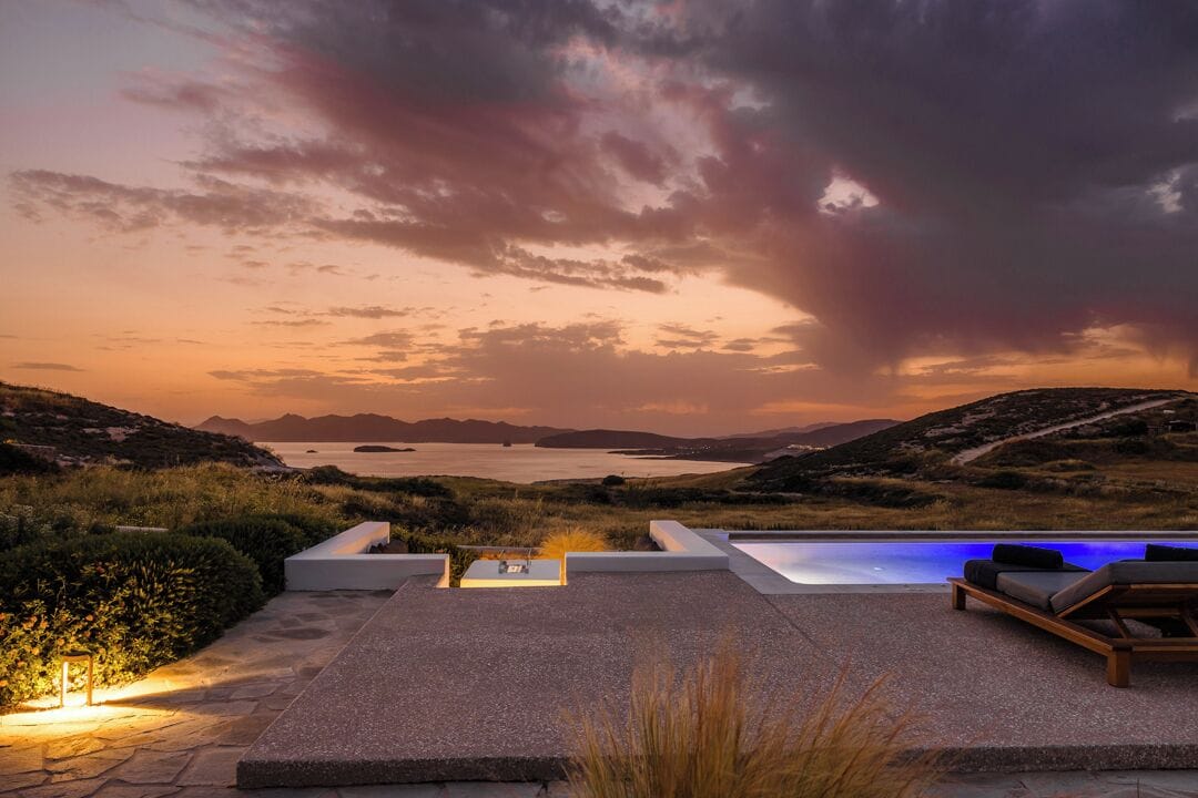 Área de piscina no terraço com vista para o mar e montanhas ao pôr do sol.