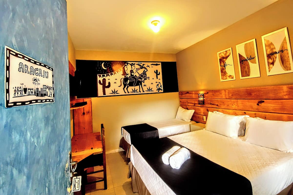 Quarto de hotel com duas camas, um painel de madeira na cabeceira e um mural na parede.