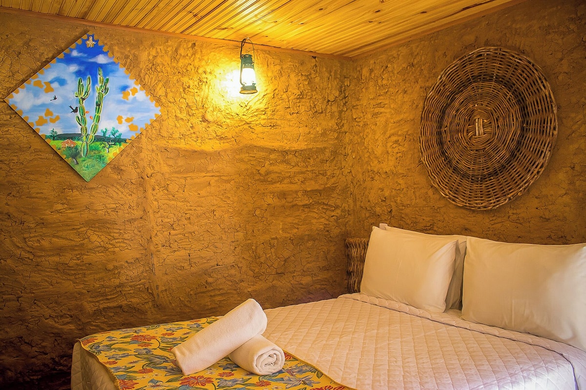 Um quarto com uma cama, um quadro, um candeeiro e um ornamento tecido na parede.