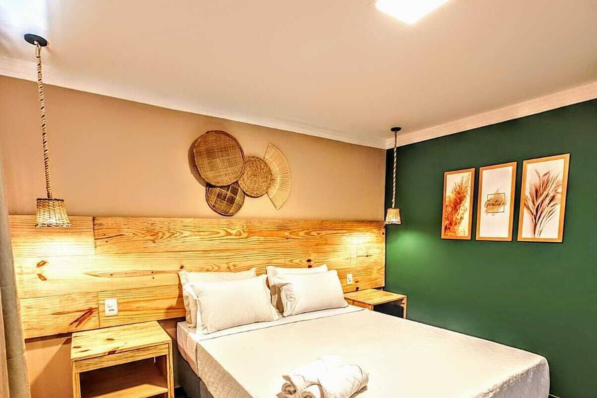 Quarto de hotel com cama, cabeceira de madeira, mesas de cabeceira e decoração na parede.