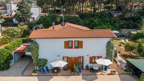 Uma casa de dois andares com telhado de telhas vermelhas, um alpendre com móveis de exterior e um jardim.