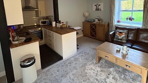 Cozinha moderna com ilha central, área de jantar com sofá e mesa de centro, e janela com vista para vegetação.