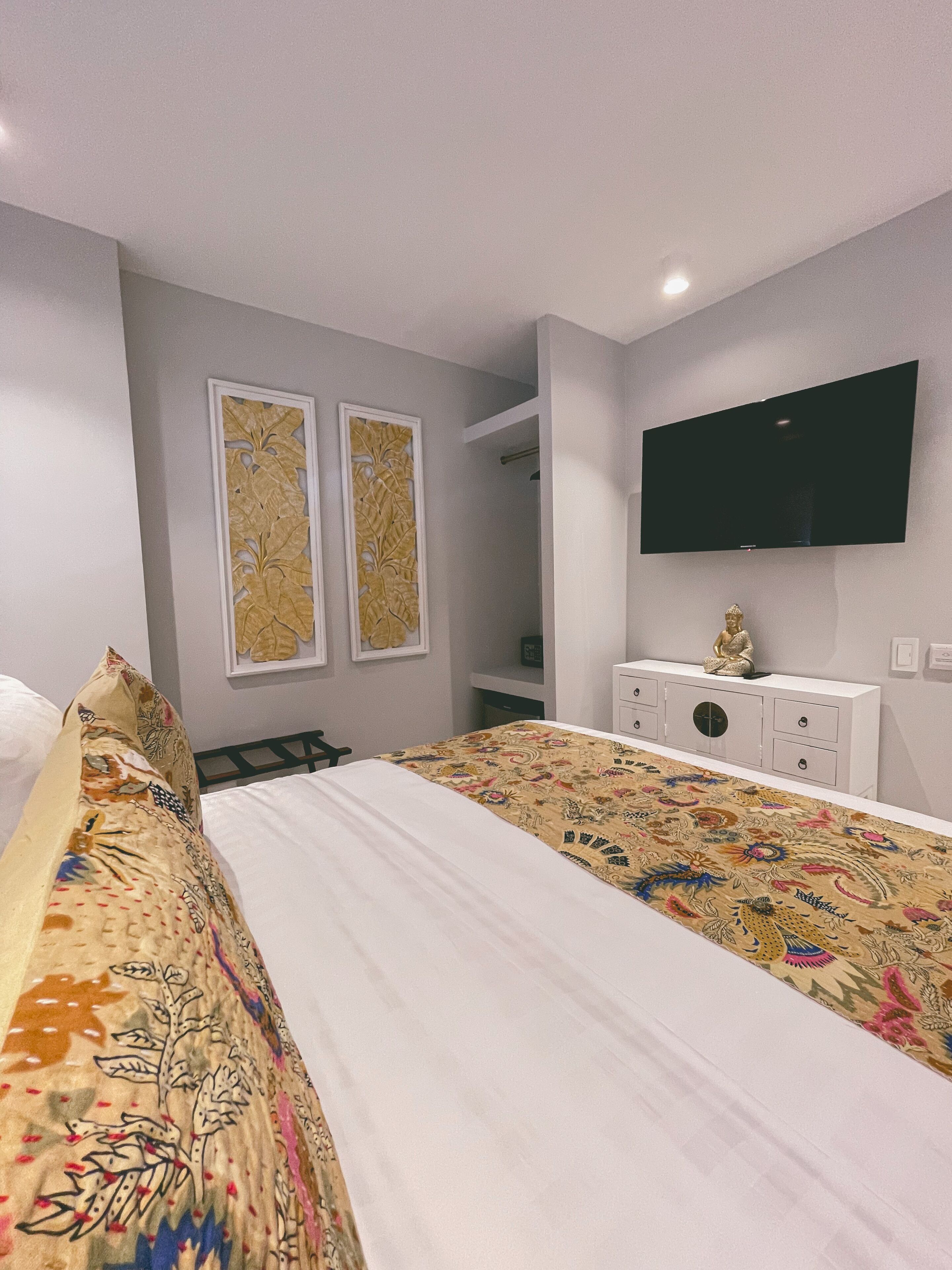Quarto moderno com uma cama grande, uma televisão de tela plana fixada na parede e dois painéis decorativos na parede.