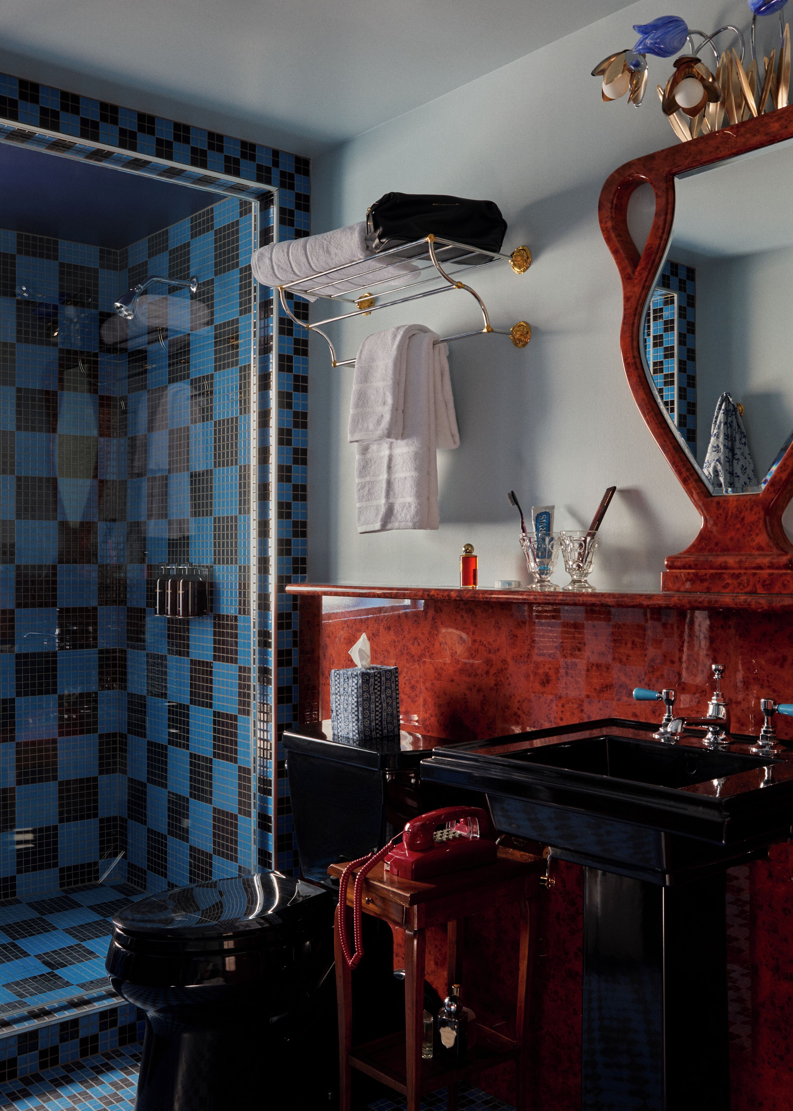 Casa de banho com parede de azulejos quadriculada em azul e preto, toucador de madeira com espelho e porta-toalhas.