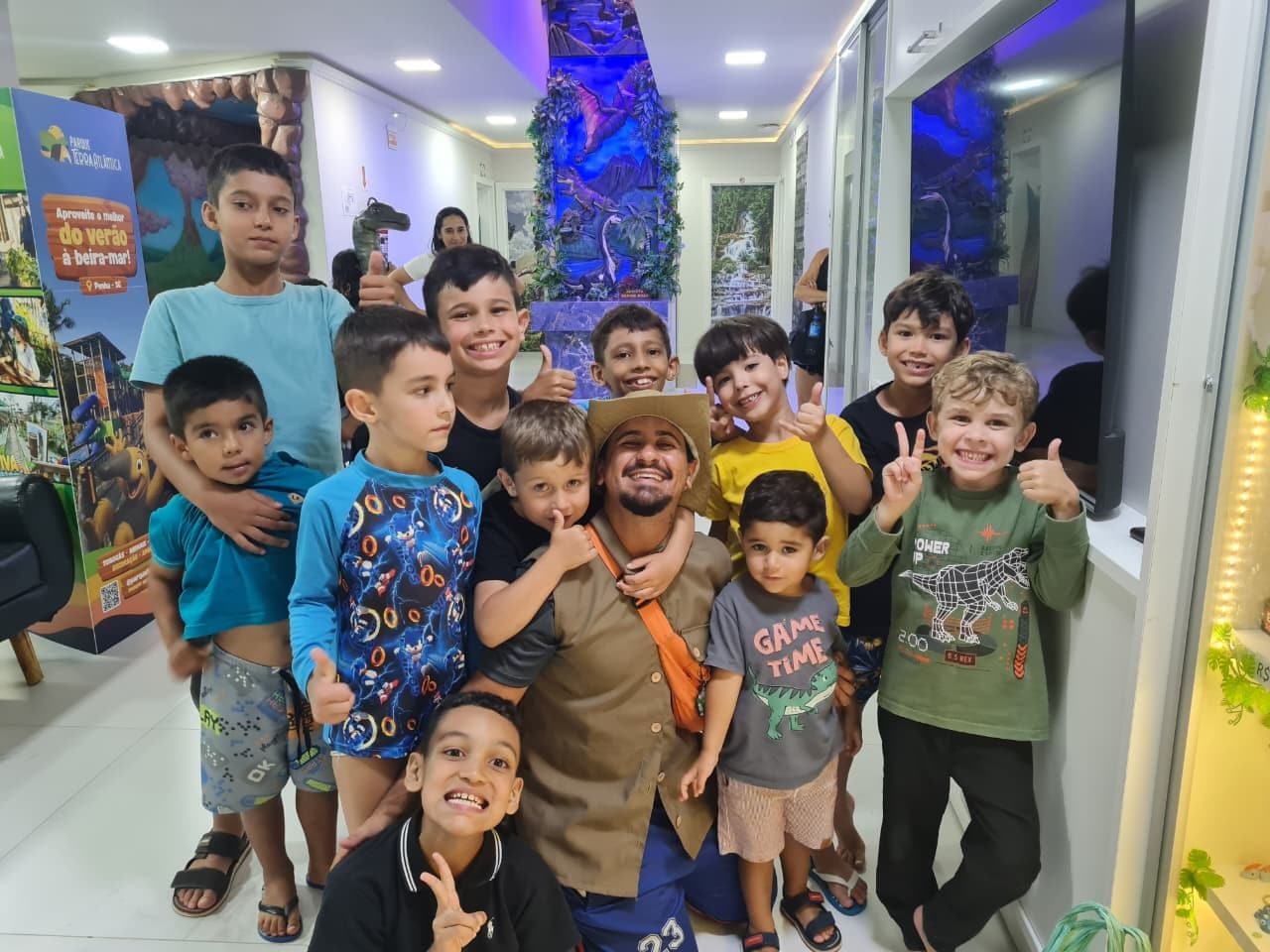 Um grupo de pessoas em um quarto com um mural de dinossauro e um pinheiro de Natal.