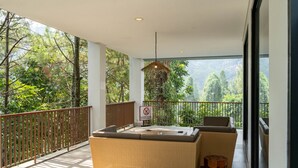 Uma varanda com móveis de vime, um candeeiro pendente e vista para uma área arborizada.