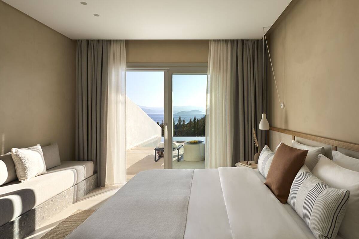 Quarto de hotel moderno com cama grande, sofá e varanda com vista para montanhas.