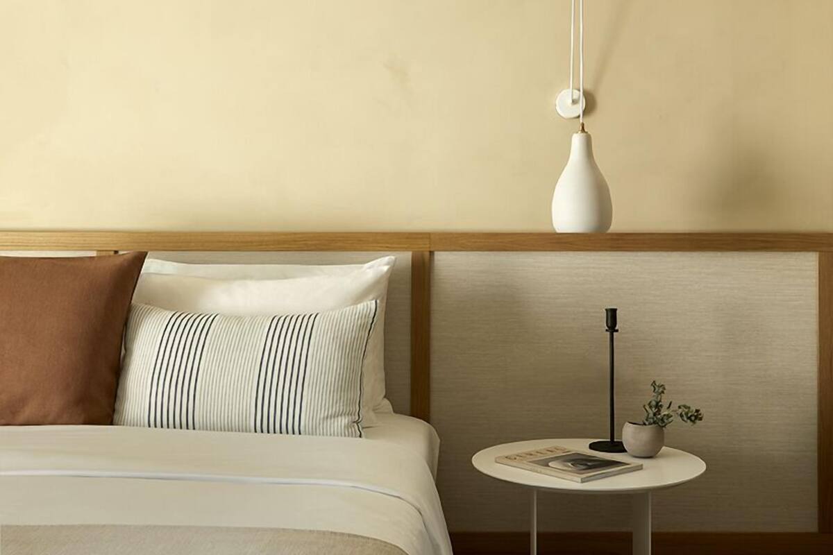 Cama bem arrumada com cabeceira, mesa de cabeceira com abajur e um pequeno vaso de planta.