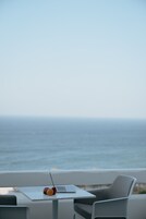 Um laptop sobre uma mesa com duas maçãs e uma chávena, com vista para uma praia e o oceano ao fundo.