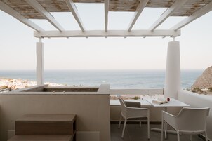 Um terraço com vista para o mar, mobiliário branco e uma estrutura de pérgula.