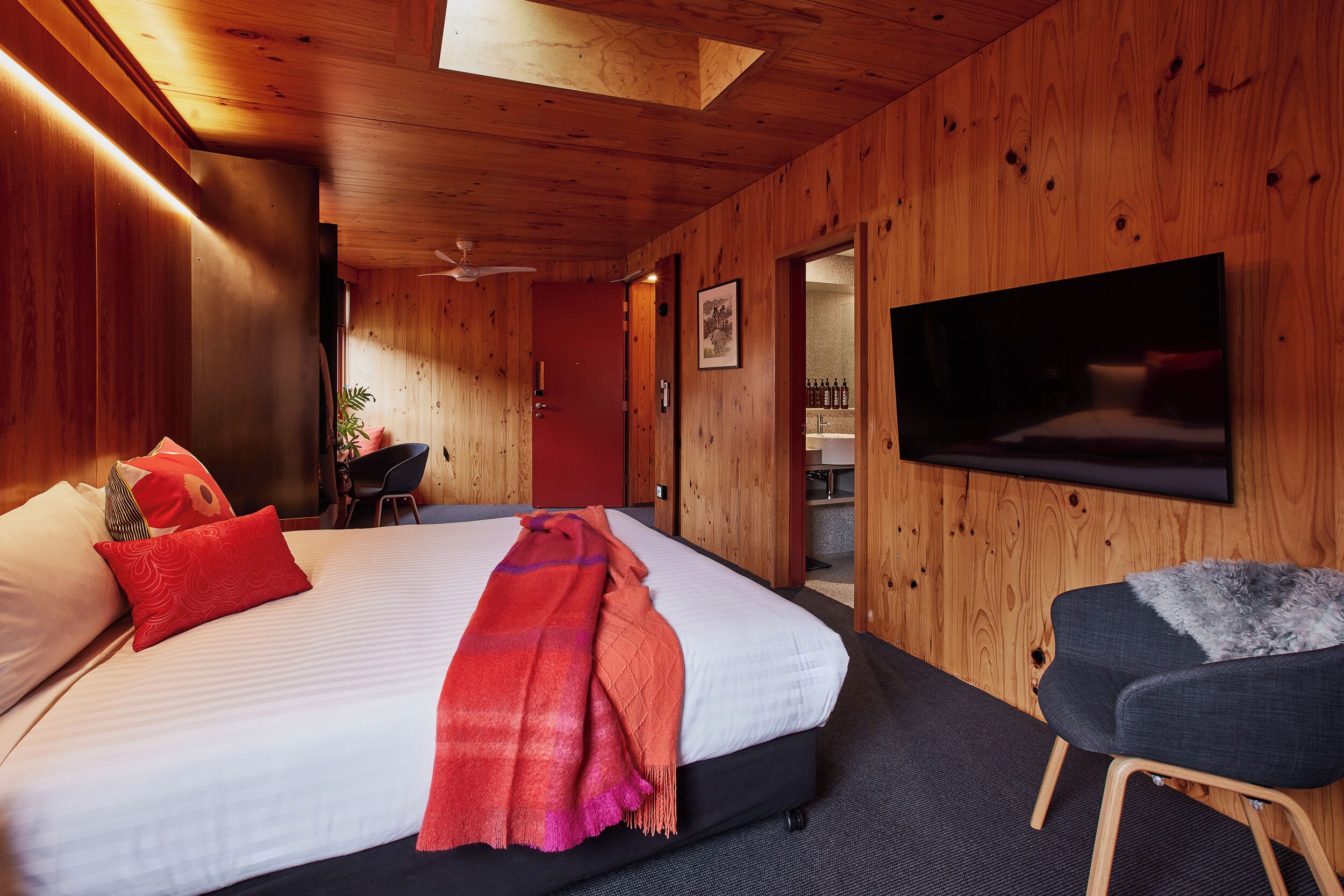 Quarto de hotel com uma cama grande, televisão de tela plana fixada na parede e teto de madeira.